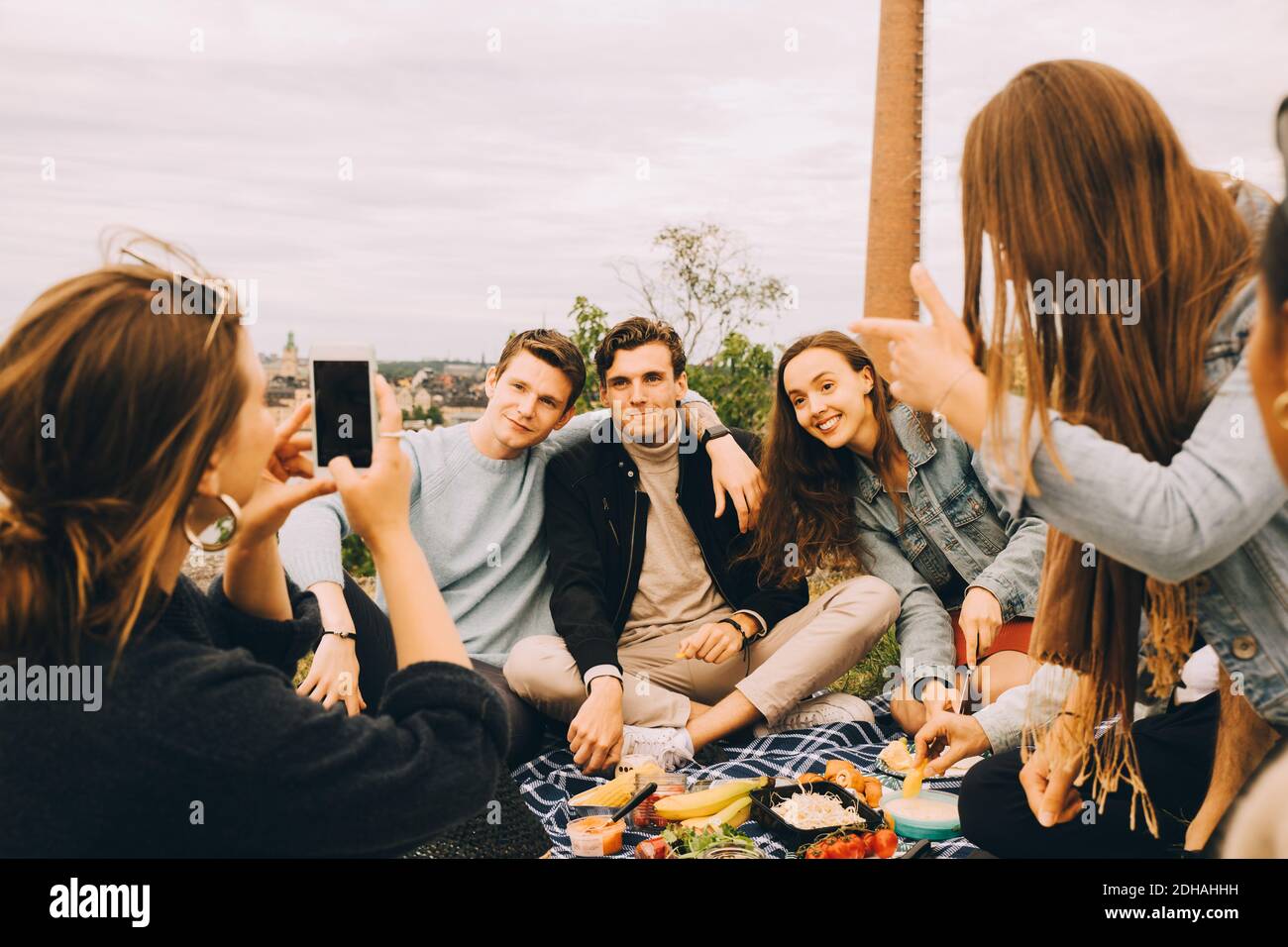 Woman photographing friends while enjoying picnic together against sky ...