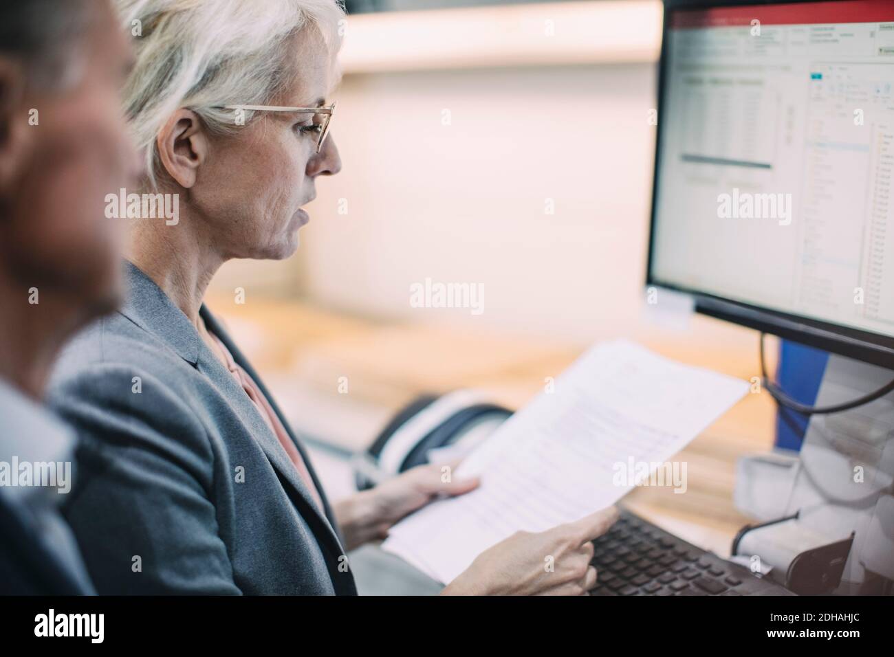 Businesswoman reading document while standing in front of desktop ...