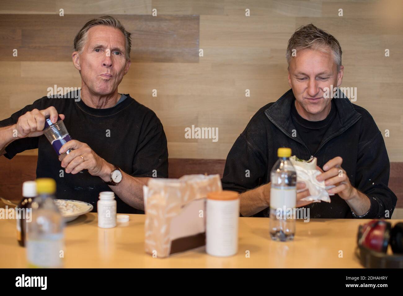 Workers eating food at table while sitting against wall during lunch ...
