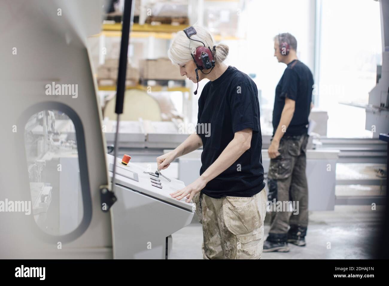 Female worker standing with colleague operating machine at industry ...