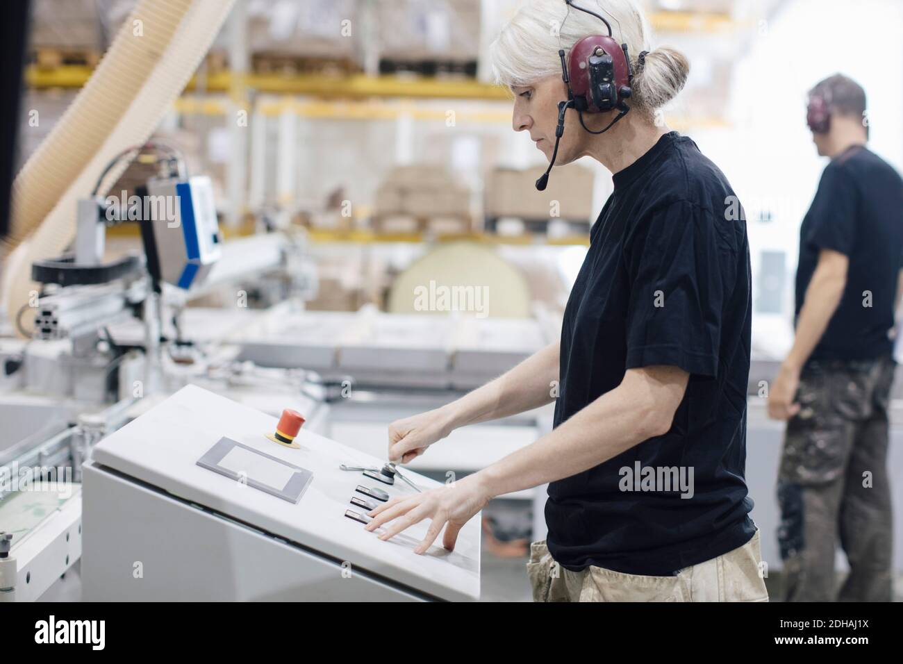 Side view of female worker wearing ear protectors operating machine at ...
