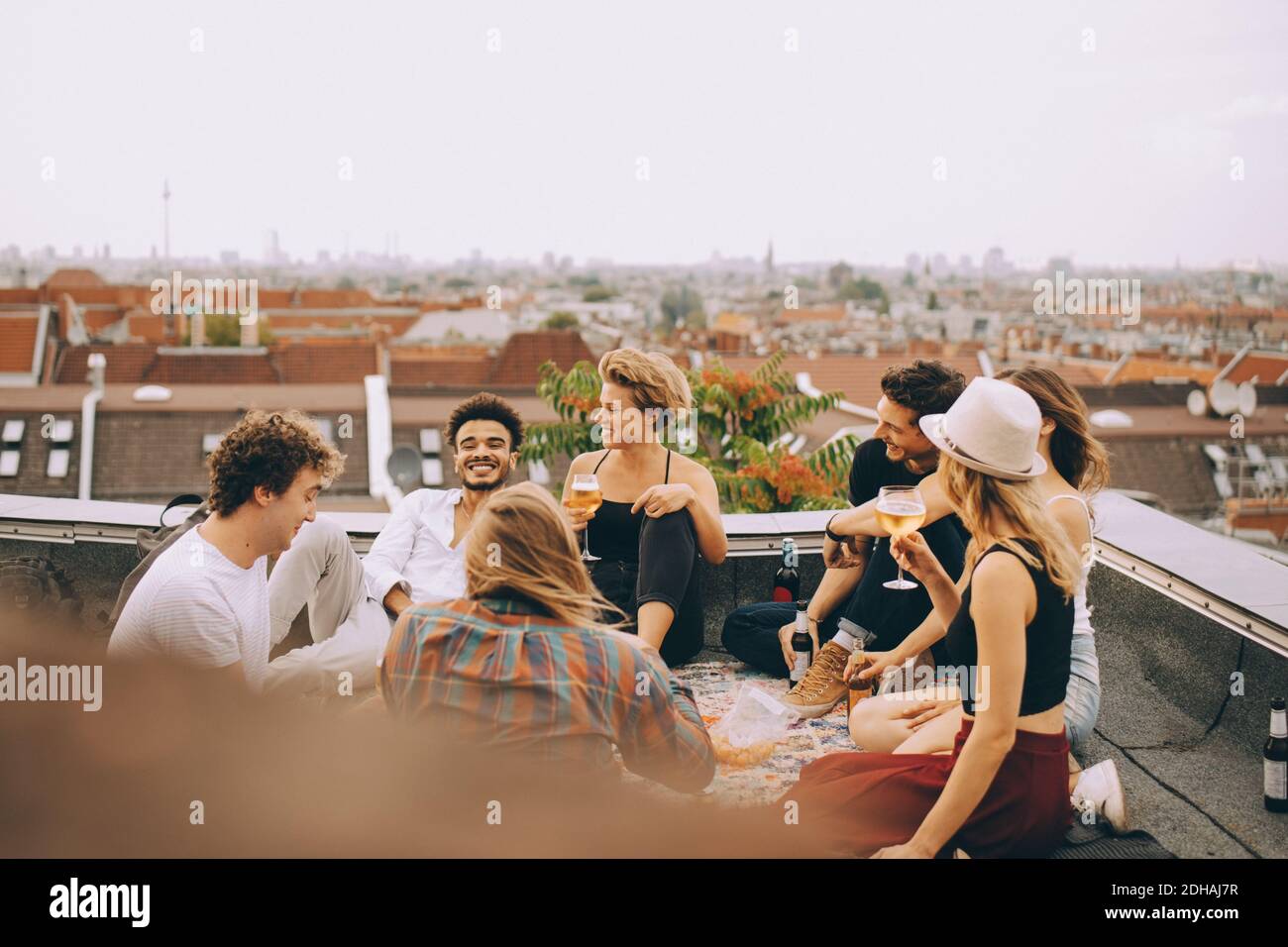 Friends enjoying beer while sitting together on terrace at rooftop ...