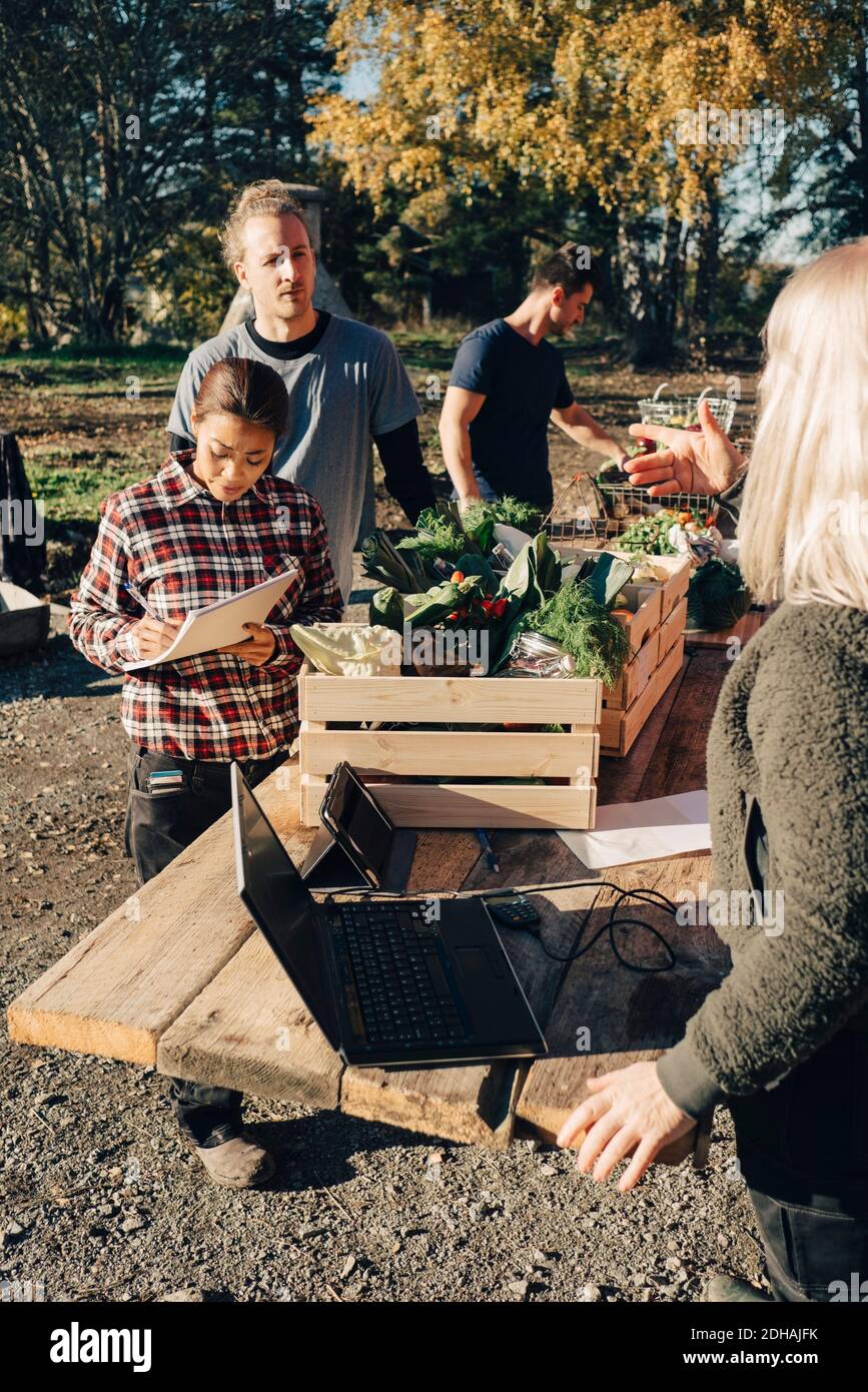 Female farmer selling organic vegetables to customers at market Stock ...