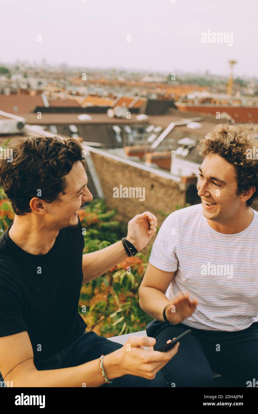 Man showing mobile phone to friend having drink at terrace during party ...