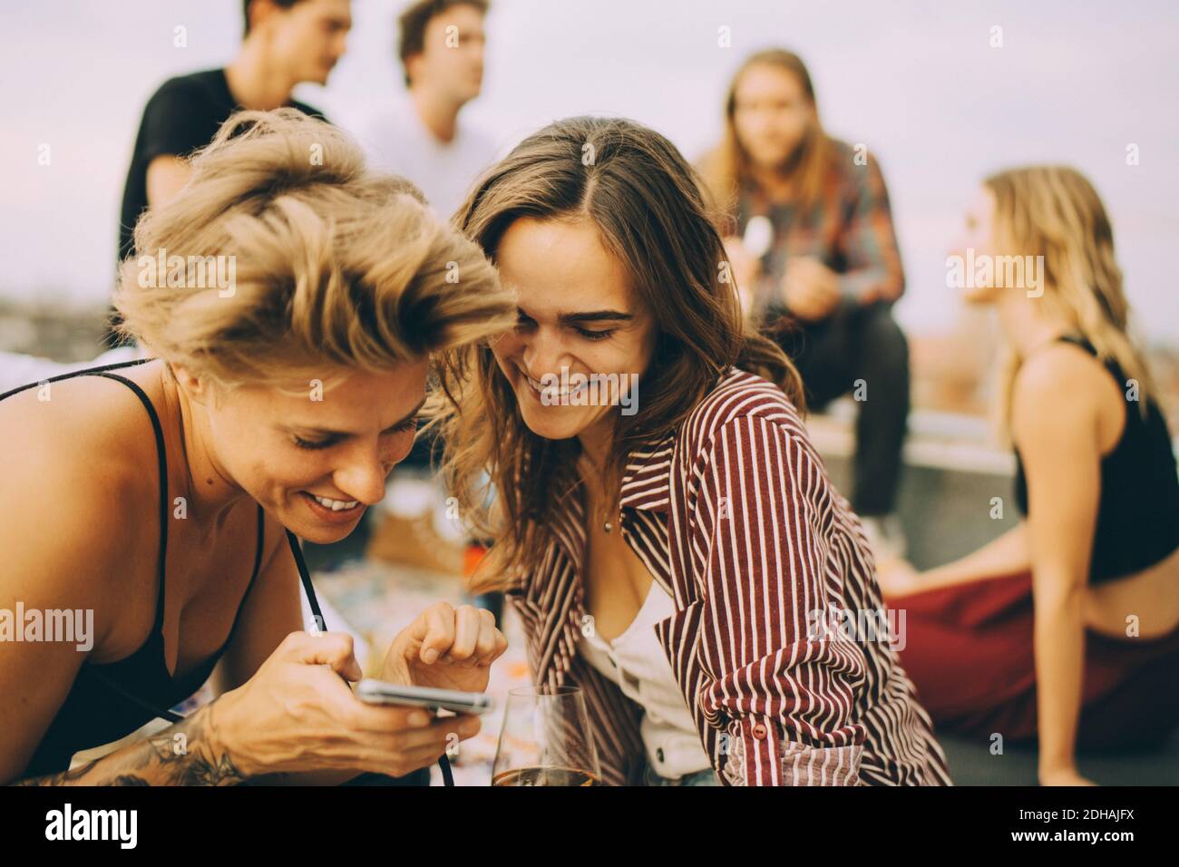 Smiling woman showing mobile phone to friend while people enjoying at ...