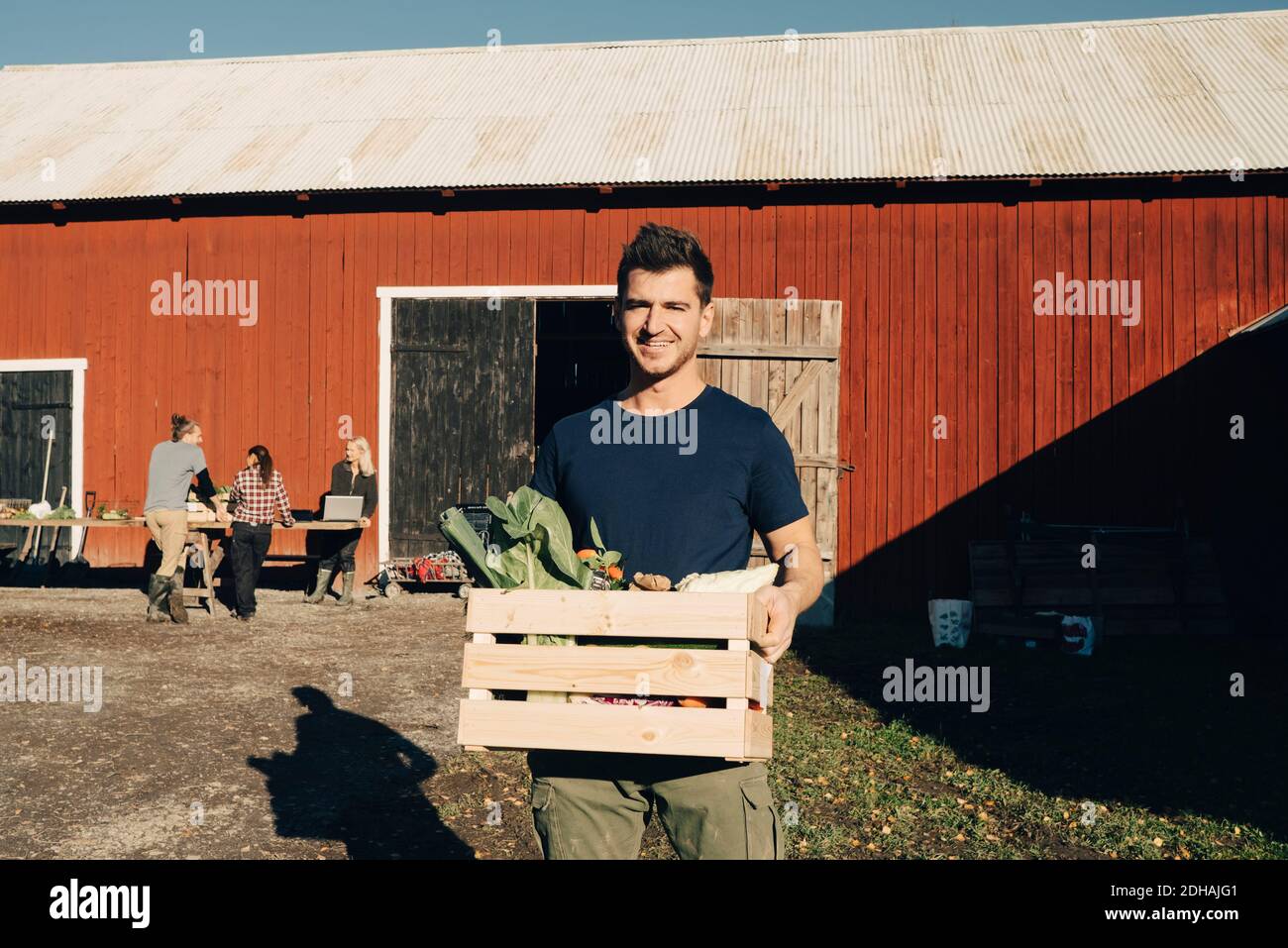 Portrait of smiling mid adult man carrying crate full of organic ...