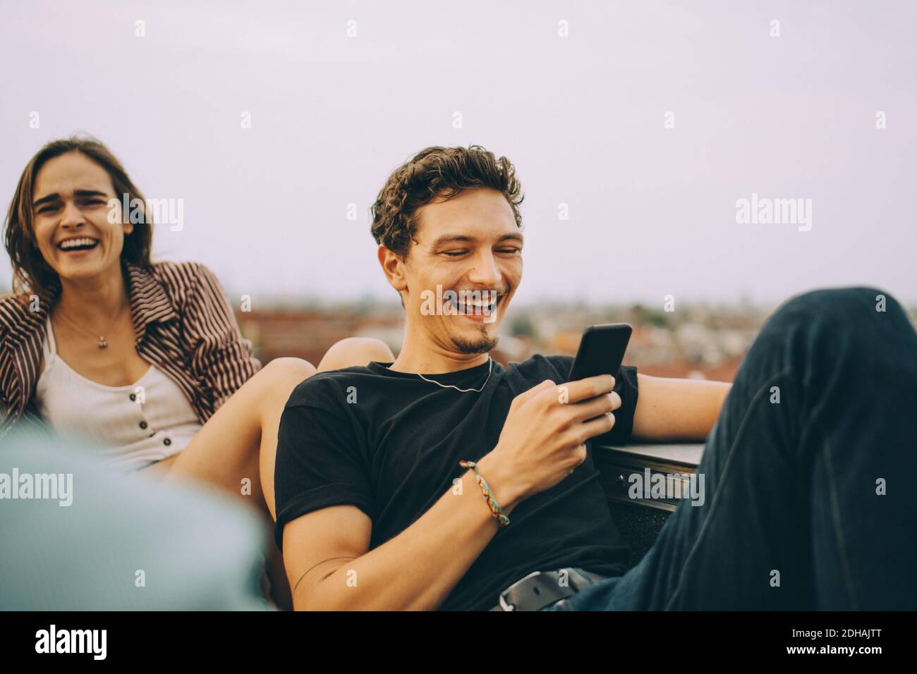 Cheerful man looking at smart phone while female friend having fun at ...