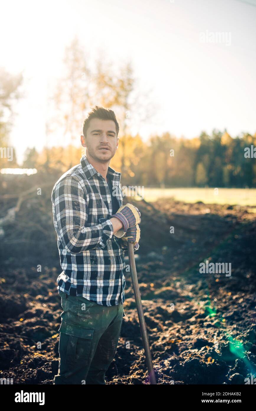 Portrait of confident male farmer with shovel standing on organic farm ...
