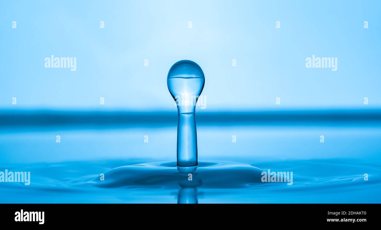 Water drop splashing into blue water surface Stock Photo - Alamy