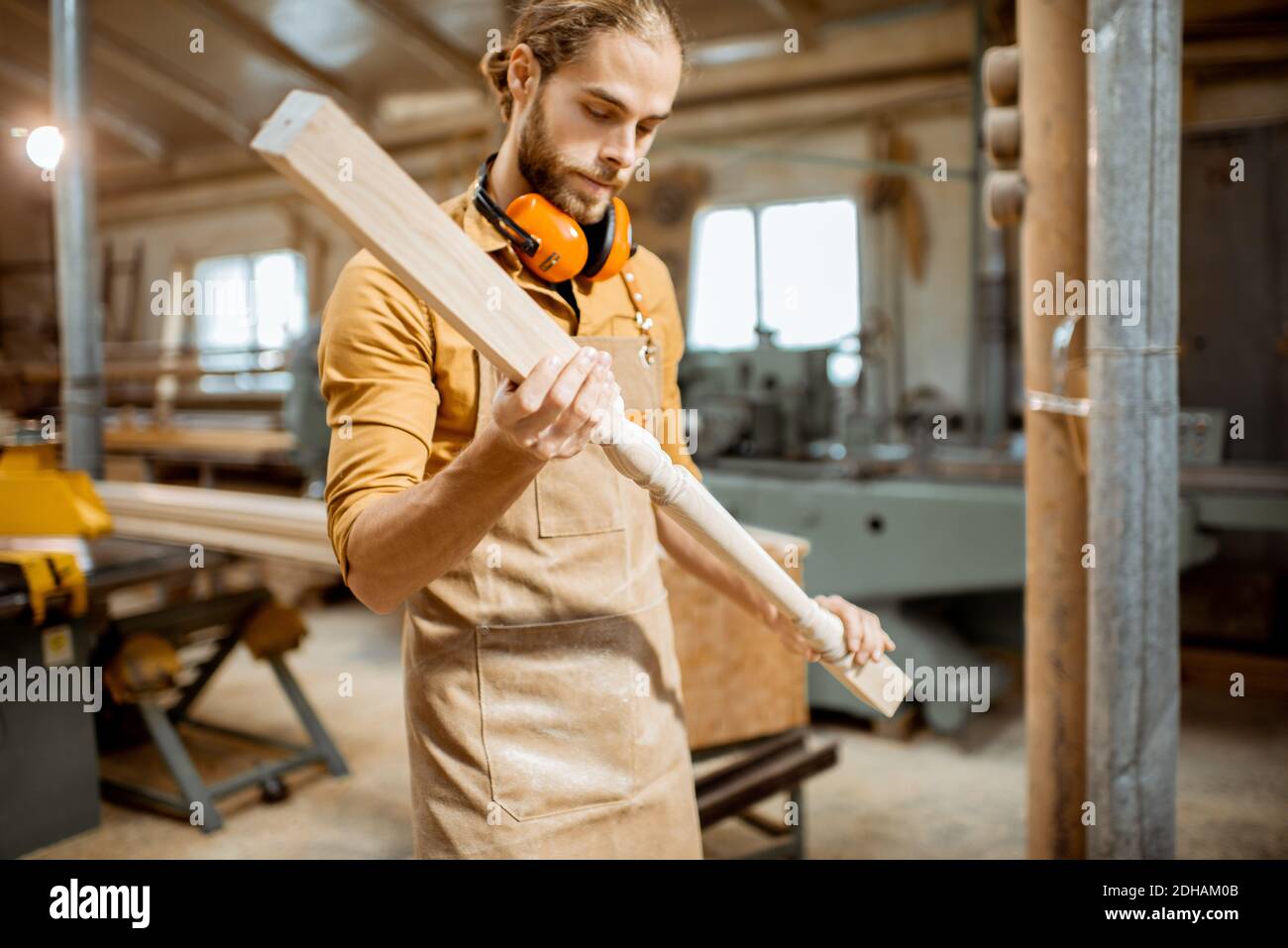 Handsome carpenter in uniform working with wood, checking the quality ...