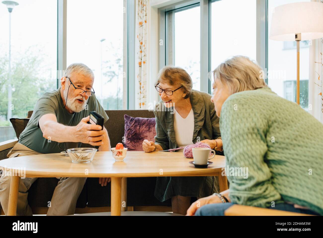 Retired elderly man sharing smart phone with friends sitting at table ...
