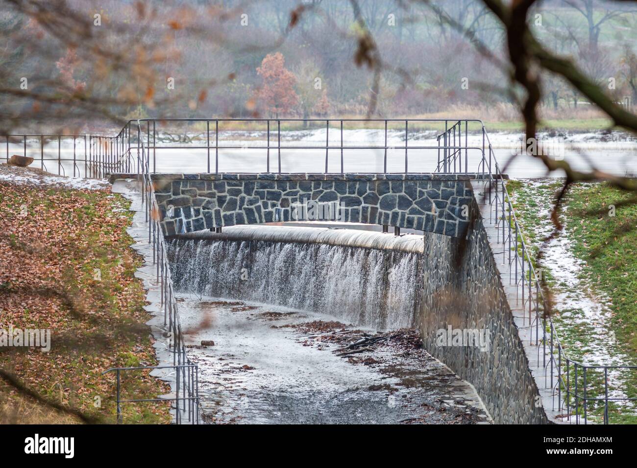 A lake embankment with outlet, a stone bridge with railing. White snow ...