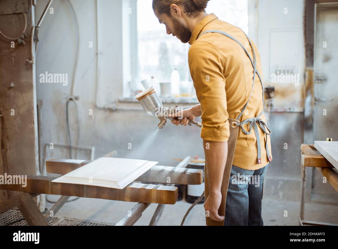 Worker painting wooden product with a spray gun at the painting shop of ...