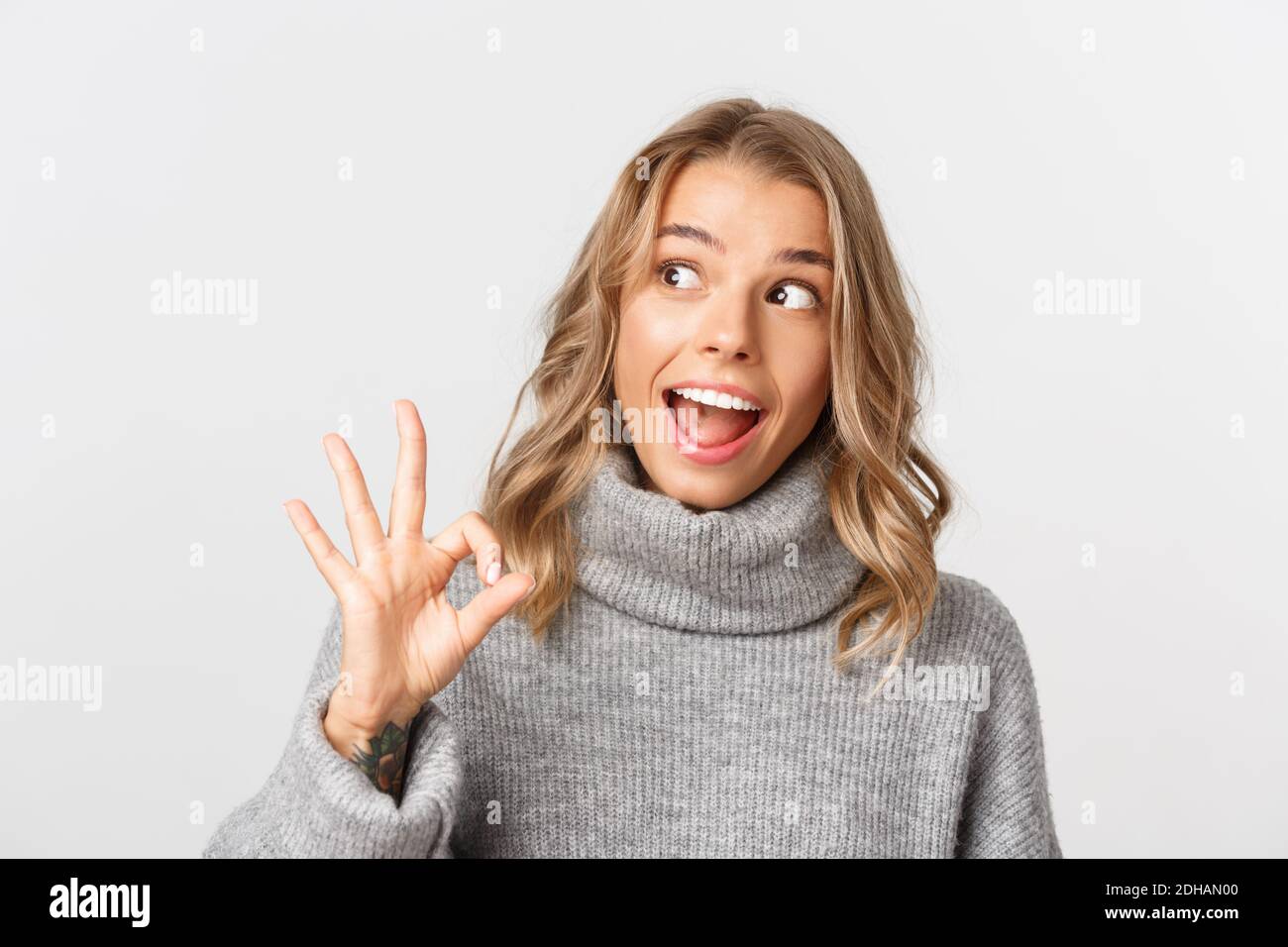 Close-up of excited blond girl in grey sweater, looking amazed left and ...