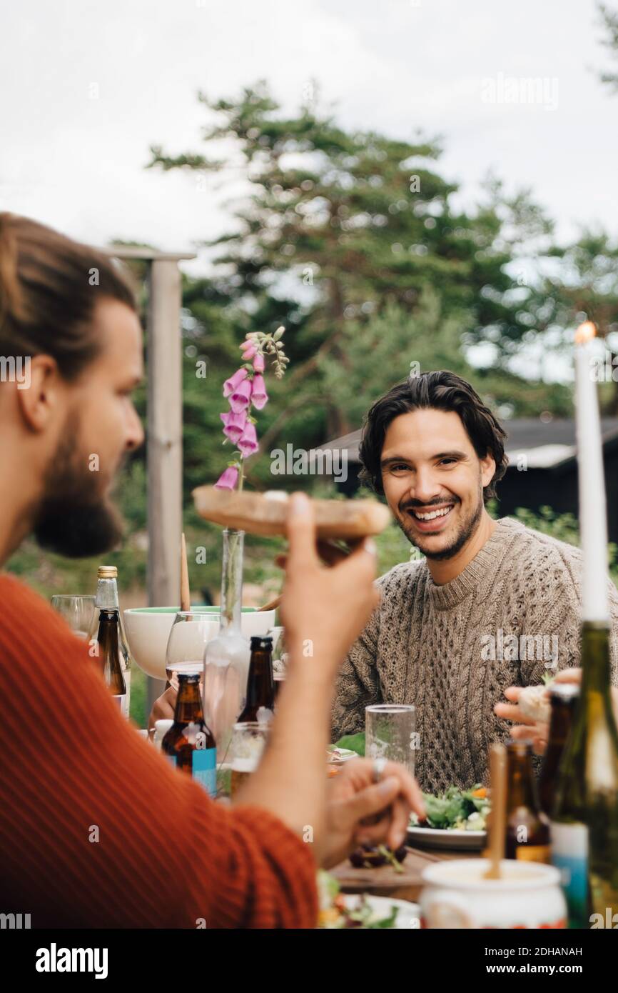 Portrait of smiling man sitting with friends at dining table in garden ...