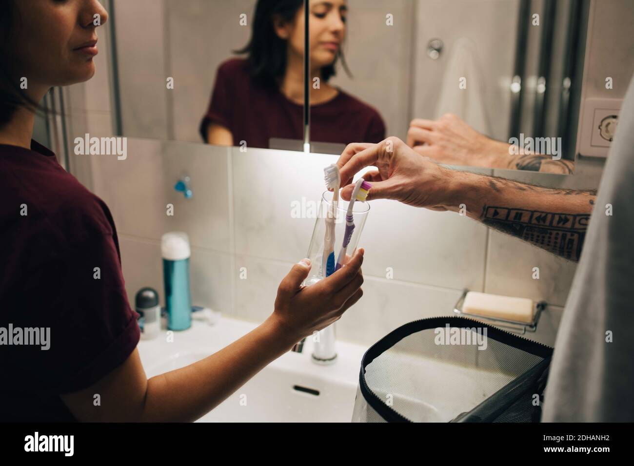 Man and woman keeping toothbrushes in container at illuminated sink ...