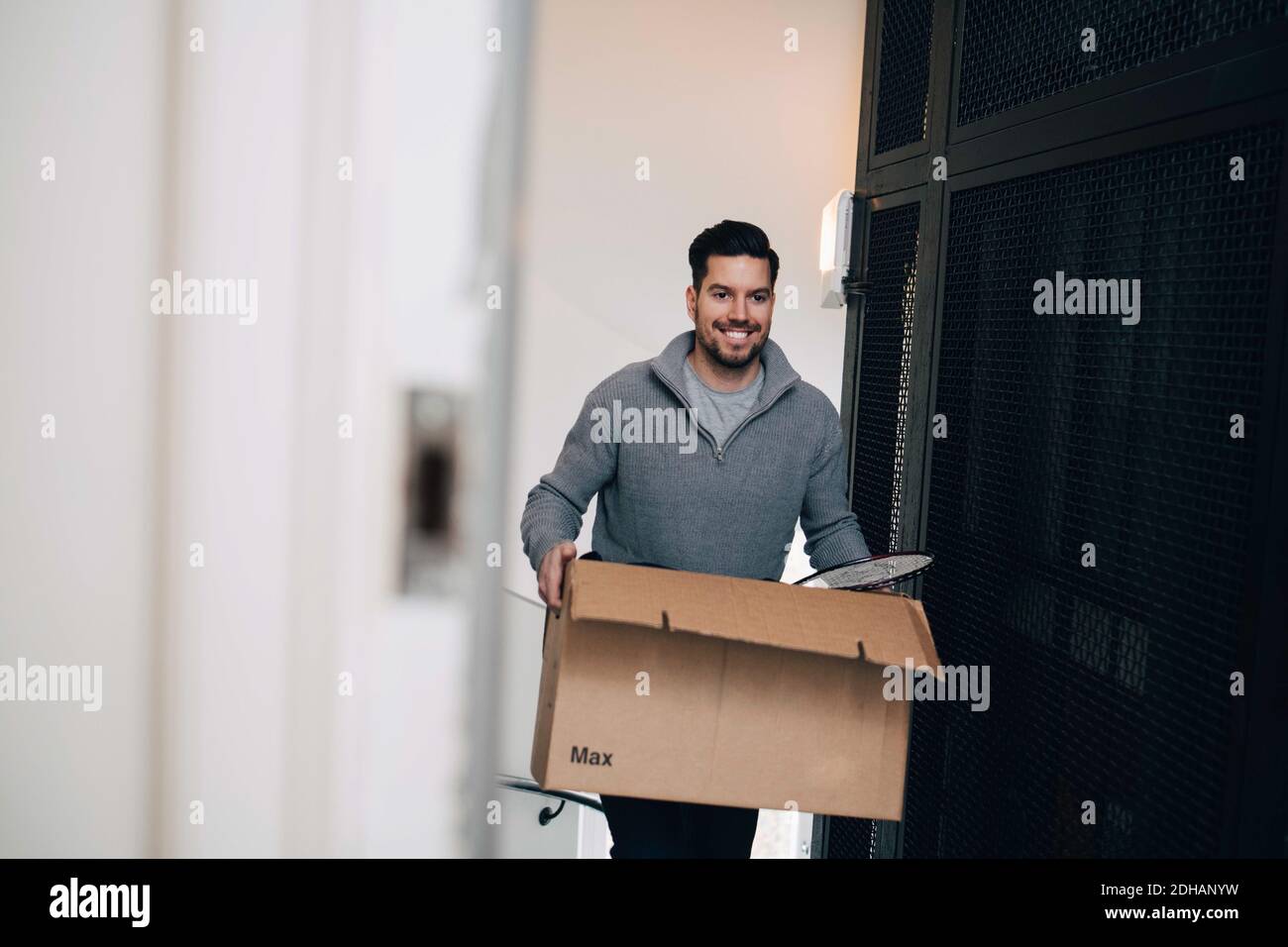 Smiling man carrying cardboard box while walking by metal grate in ...