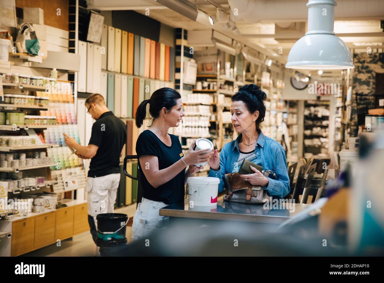 Sales woman showing paint can to customer at hardware store Stock Photo ...