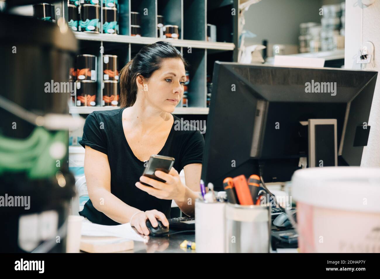 Sales woman using computer while holding mobile phone in store Stock ...