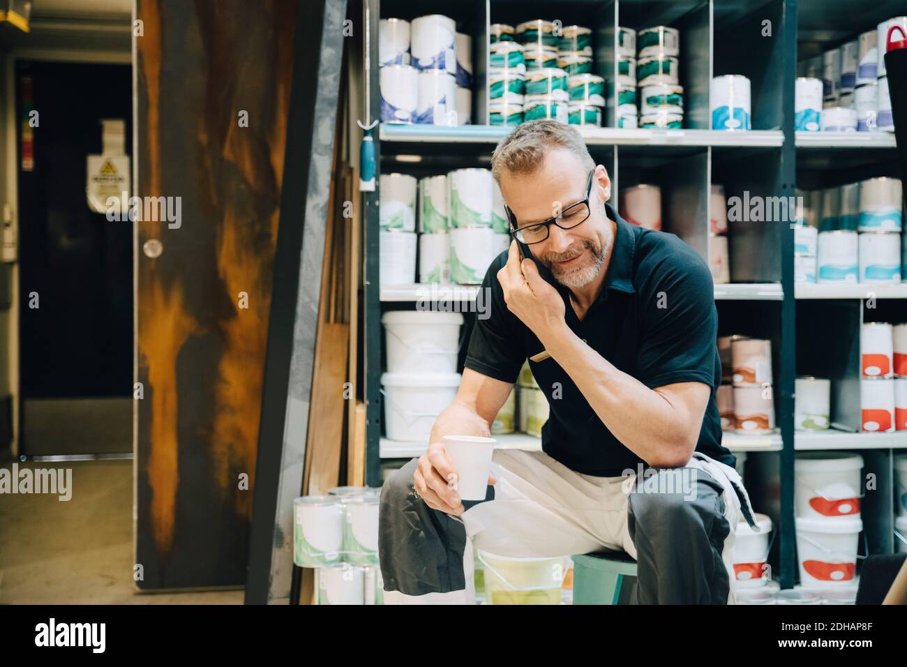 Salesman using phone while sitting on stool in storage room Stock Photo ...
