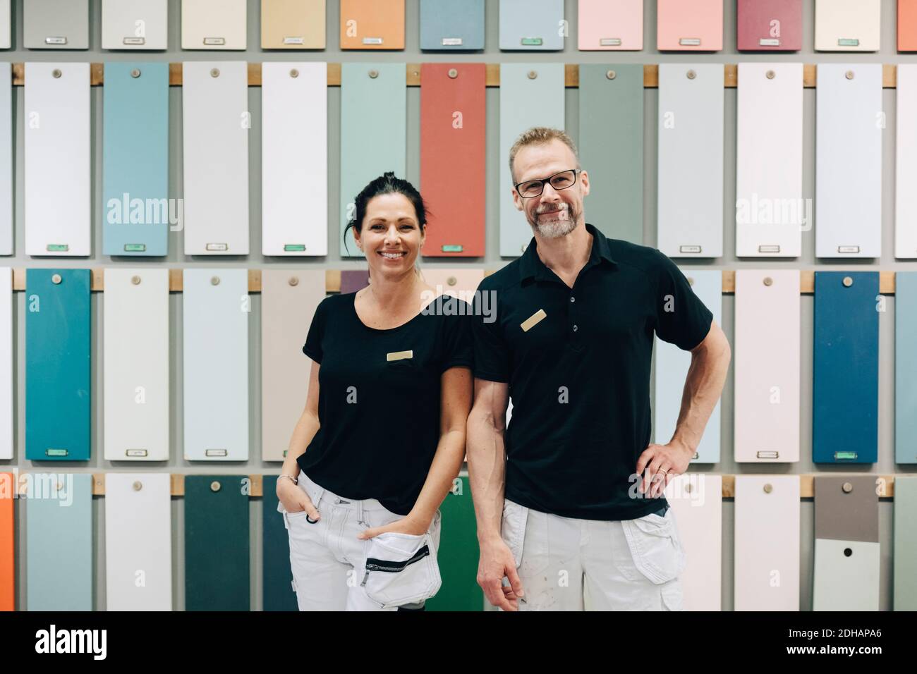 Portrait of smiling sales employees standing against multi colored wall ...