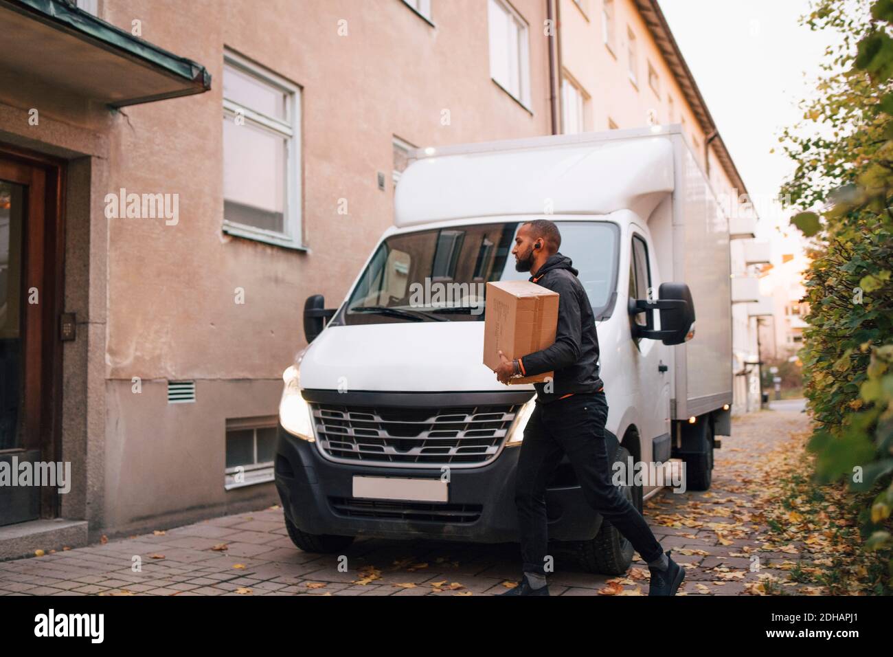 Side view of man carrying box while walking by delivery van in city ...