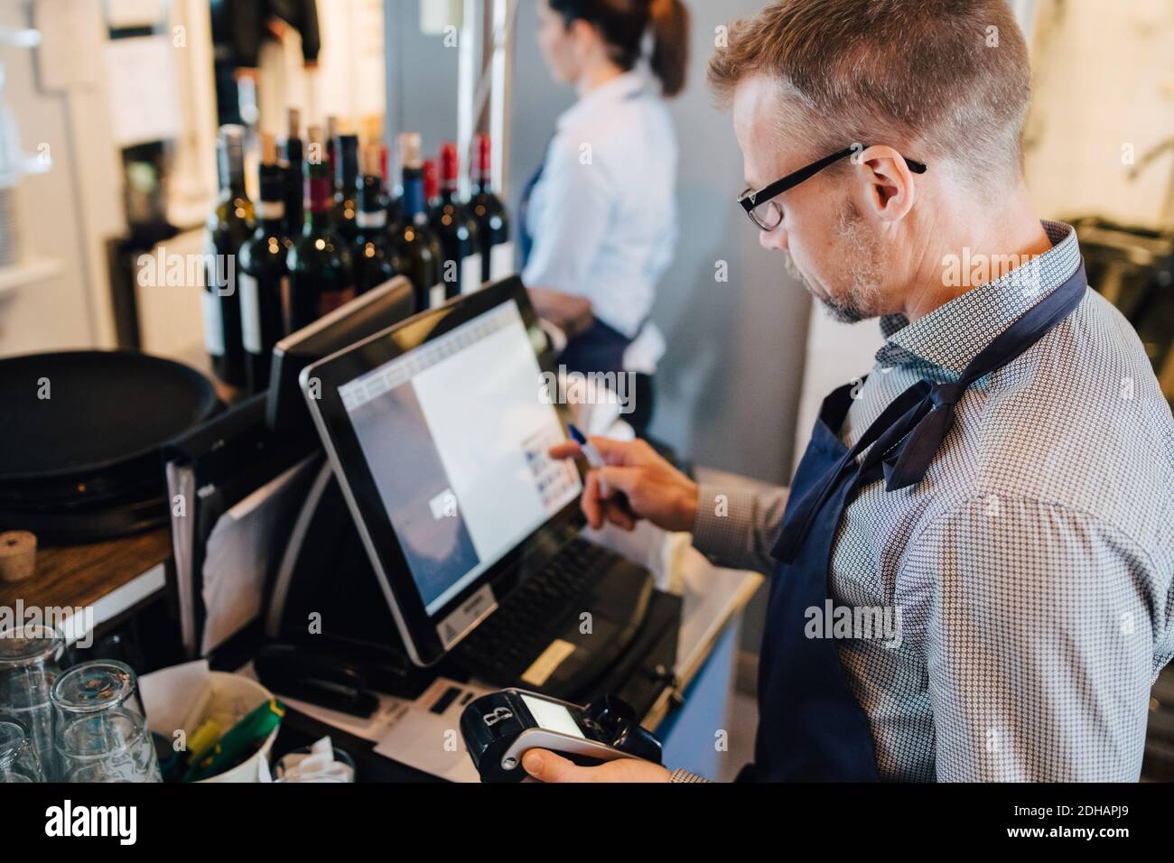 Owner using computer while holding credit card reader in restaurant ...