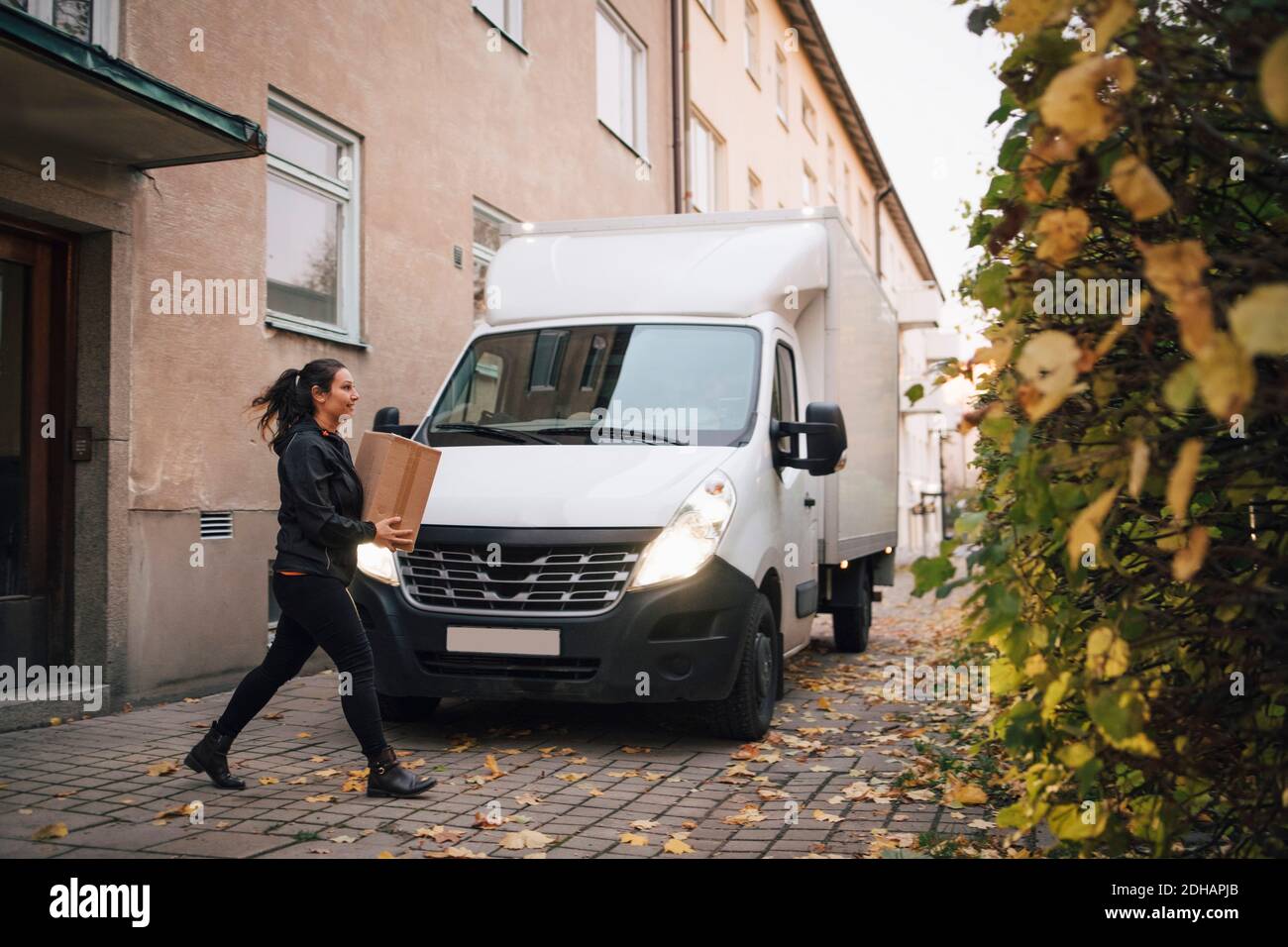 Side view of worker carrying box while walking by delivery van in city ...