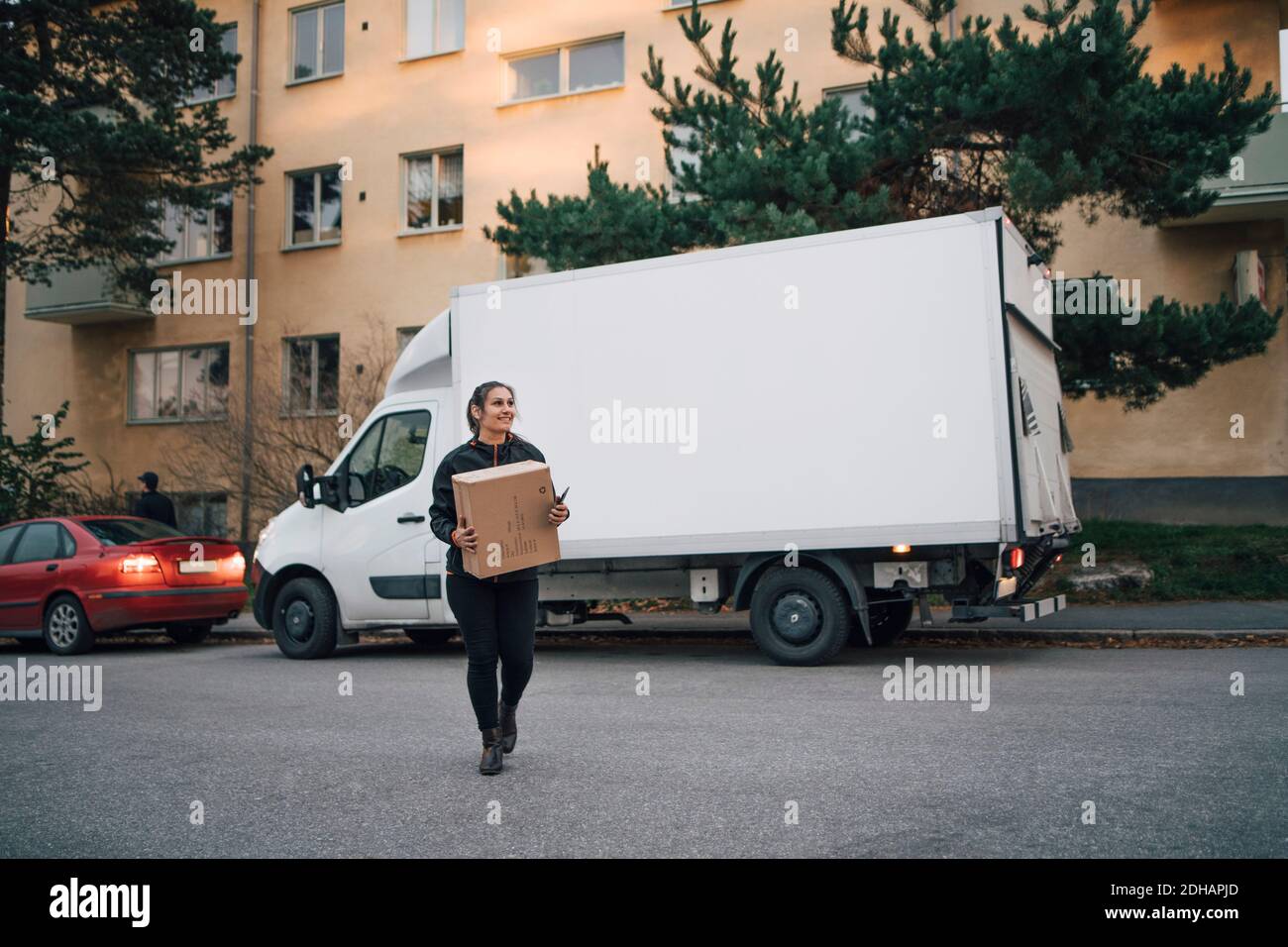 Full length of female worker carrying box while walking against ...