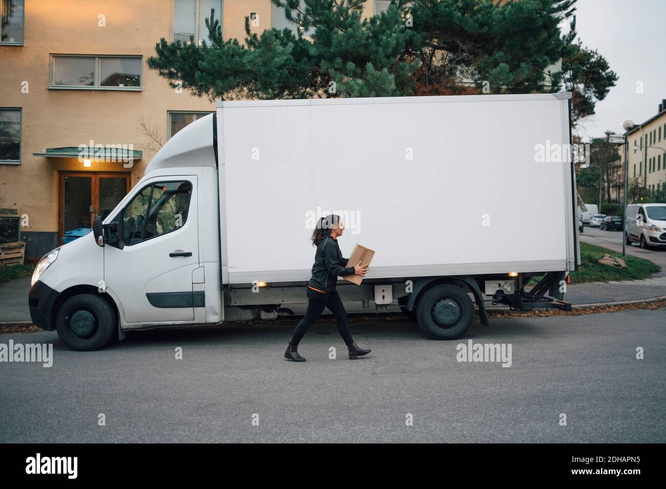 Female worker carrying box while walking by delivery van on street in ...
