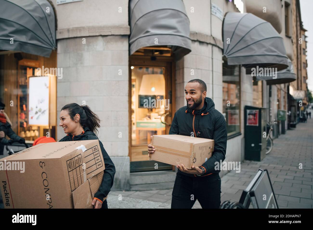 Smiling male and female workers carrying cardboard boxes while walking ...
