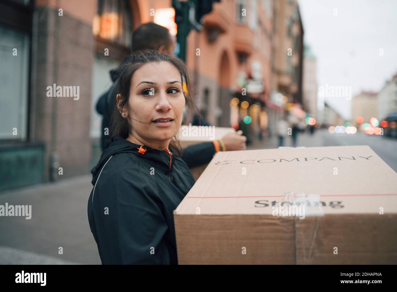 Thoughtful woman carrying box while walking with coworker in city ...