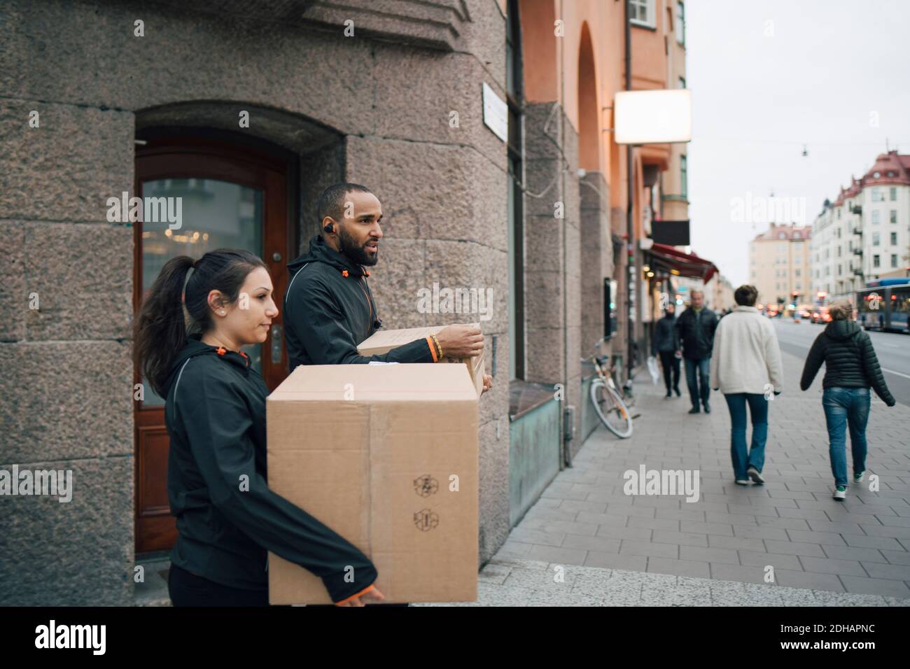 Male and female workers carrying cardboard boxes while walking in city ...