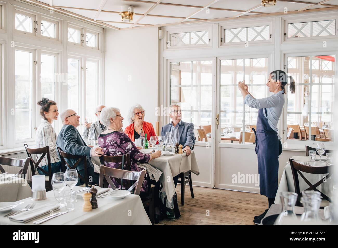 Owner clicking photograph of Senior friends sitting in restaurant Stock ...