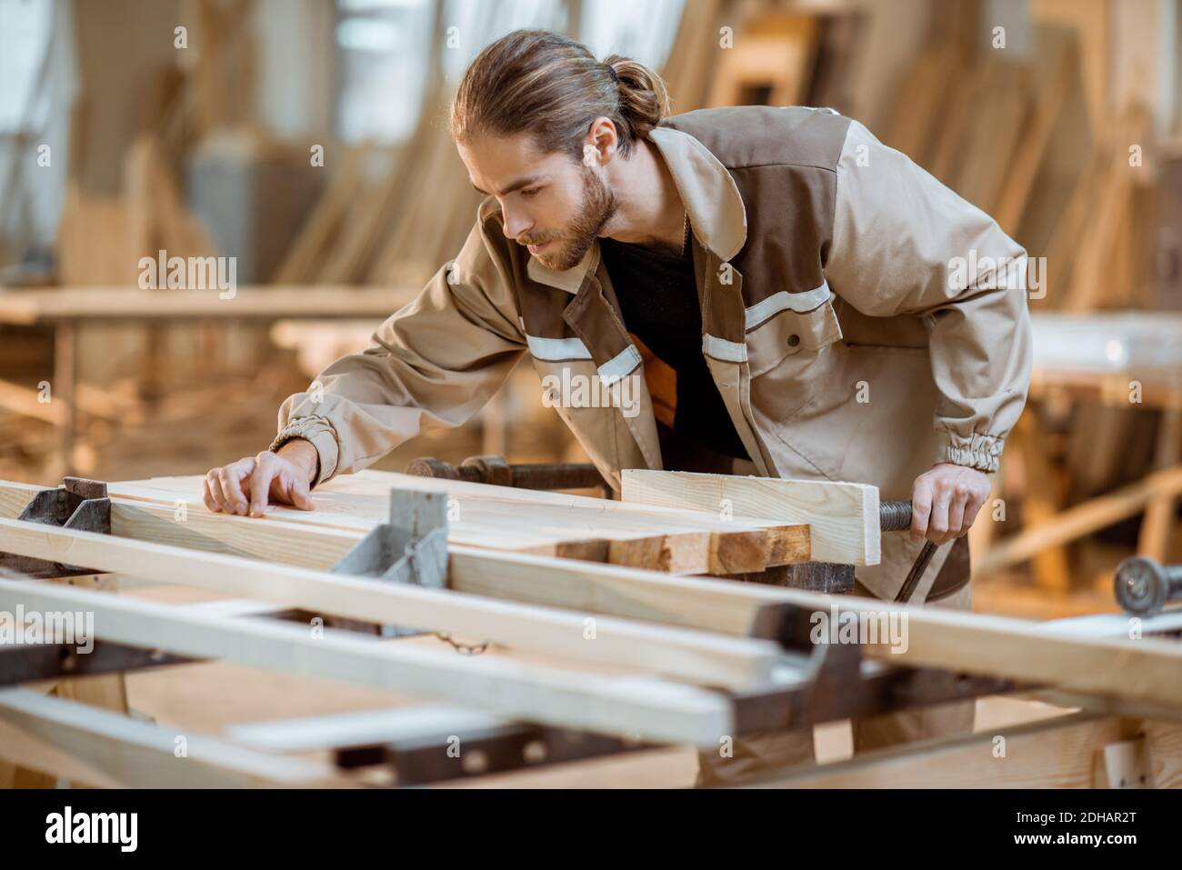Handsome carpenter in uniform gluing wooden bars with hand pressures at ...