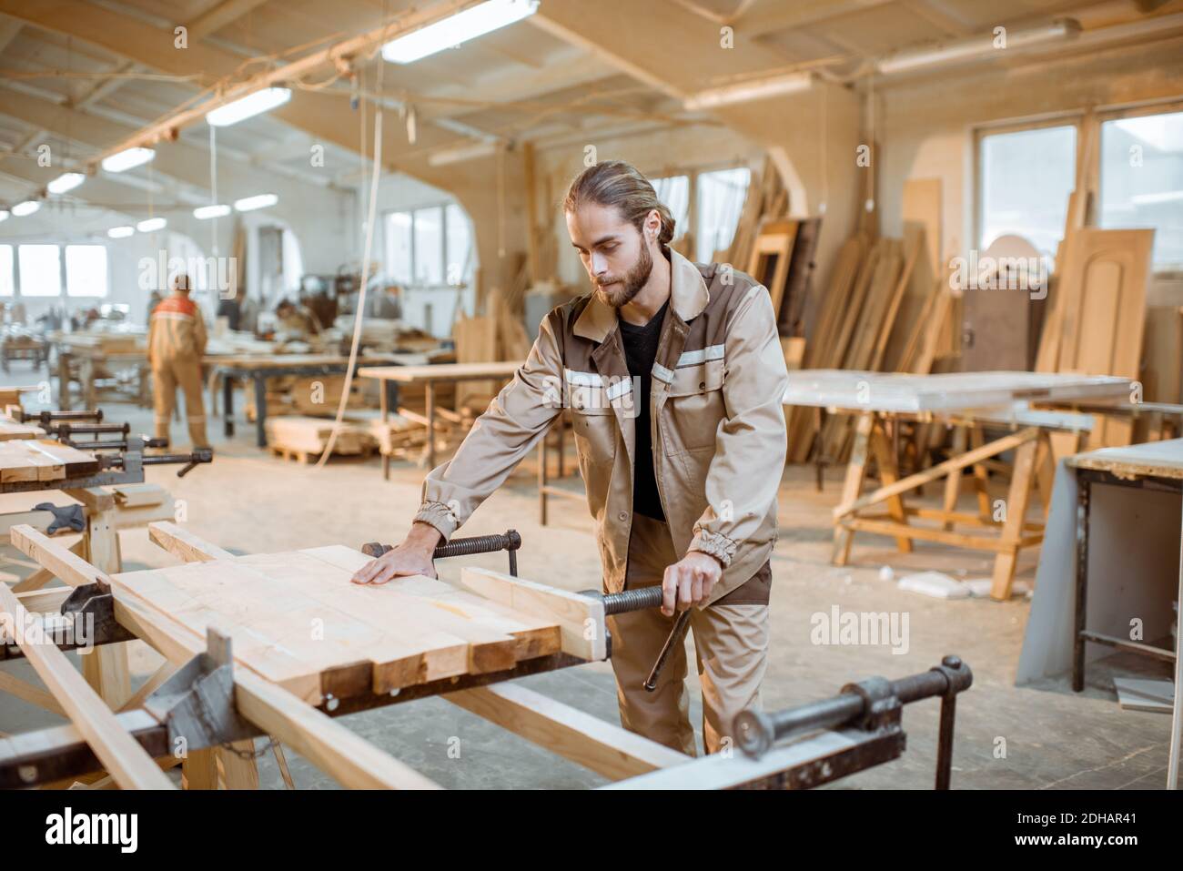 Handsome carpenter in uniform gluing wooden bars with hand pressures at ...