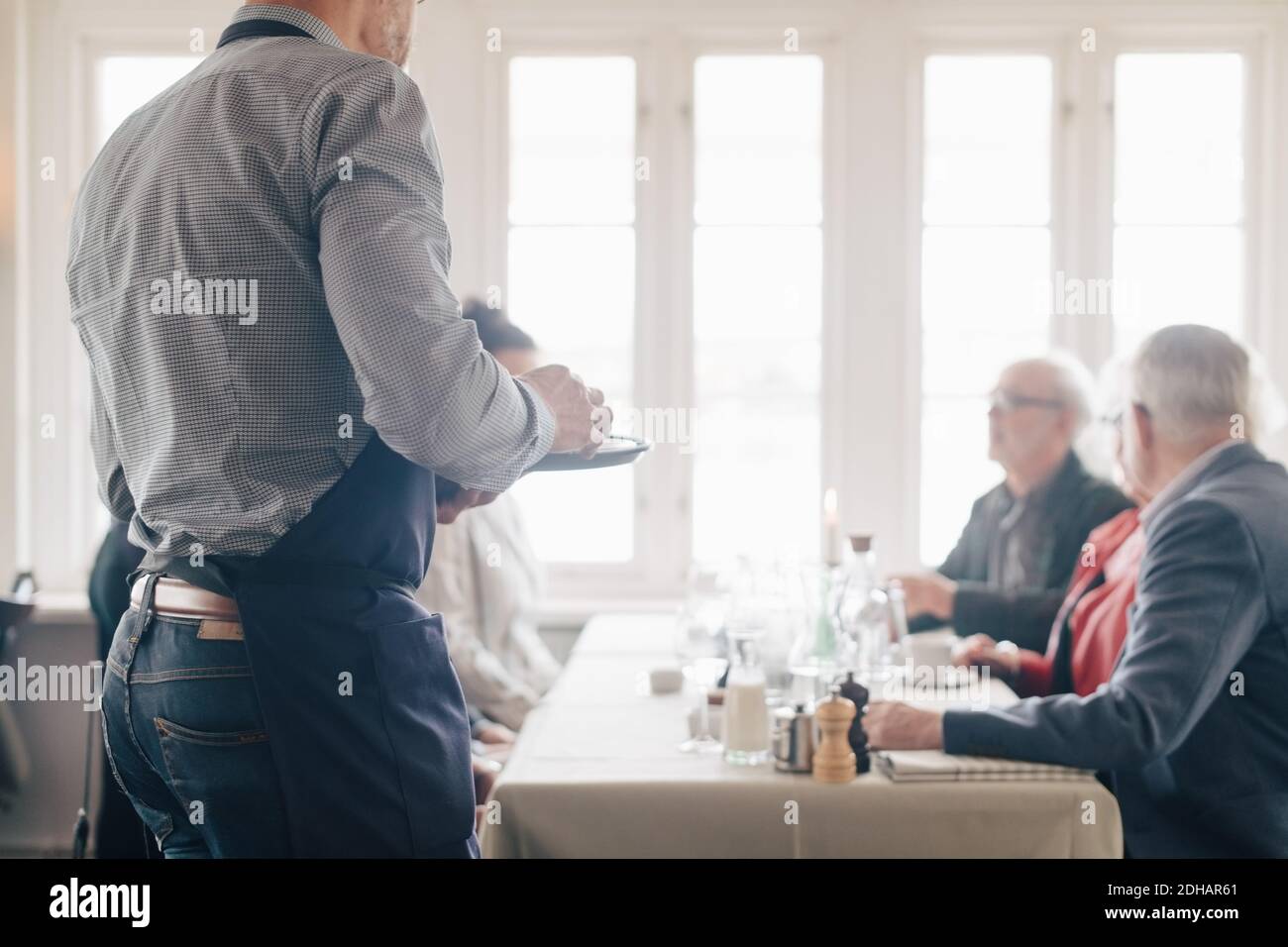 Midsection of owner standing by table while male and female sitting in ...