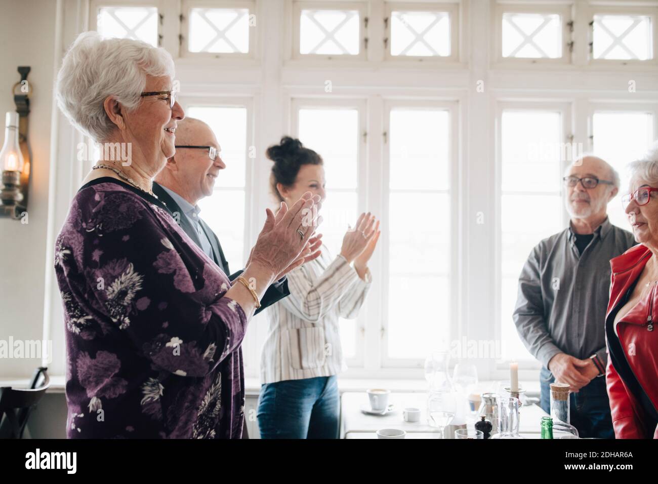 Male and female friends clapping hands while standing by table in ...