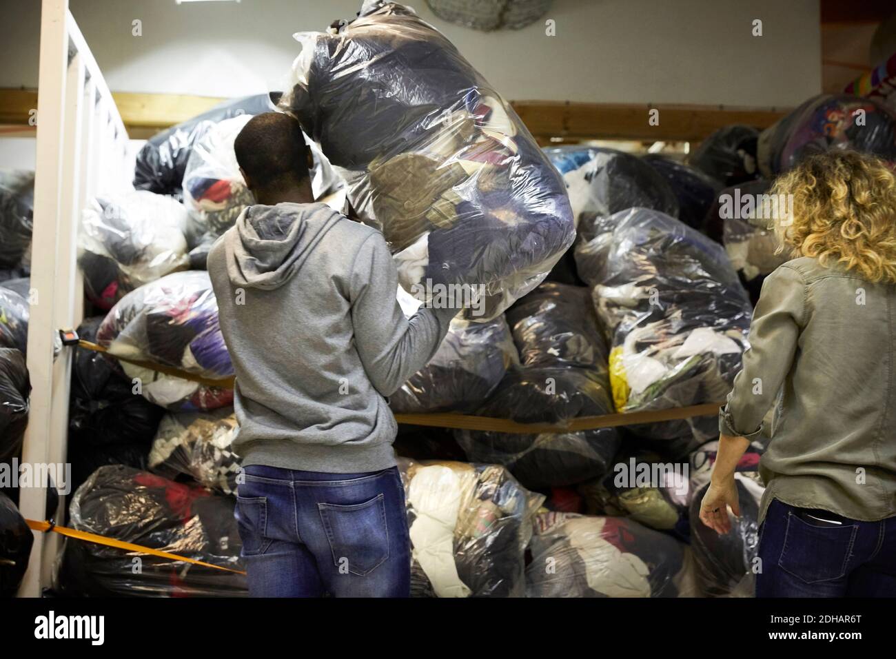 Rear view of coworkers stacking plastic sacks in warehouse Stock Photo ...