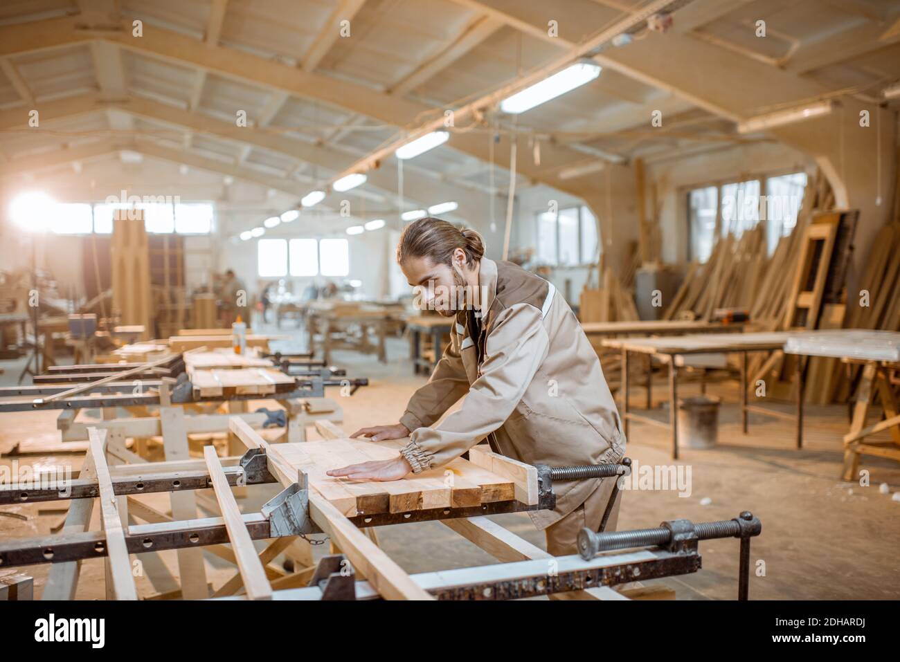 Handsome carpenter in uniform gluing wooden bars with hand pressures at ...