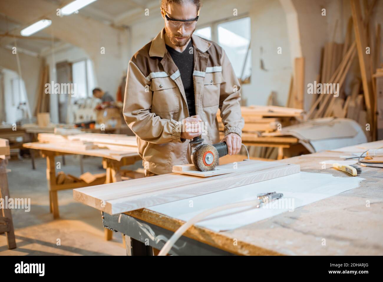 Handsome carpenter in uniform brushing wood with hand machine at the ...