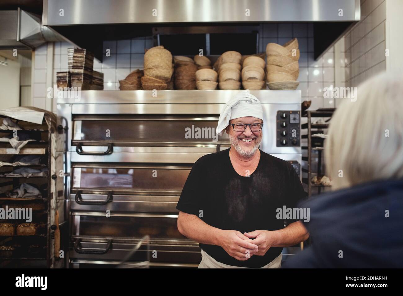 Smiling senior male baker standing against cooling rack at bakery Stock ...