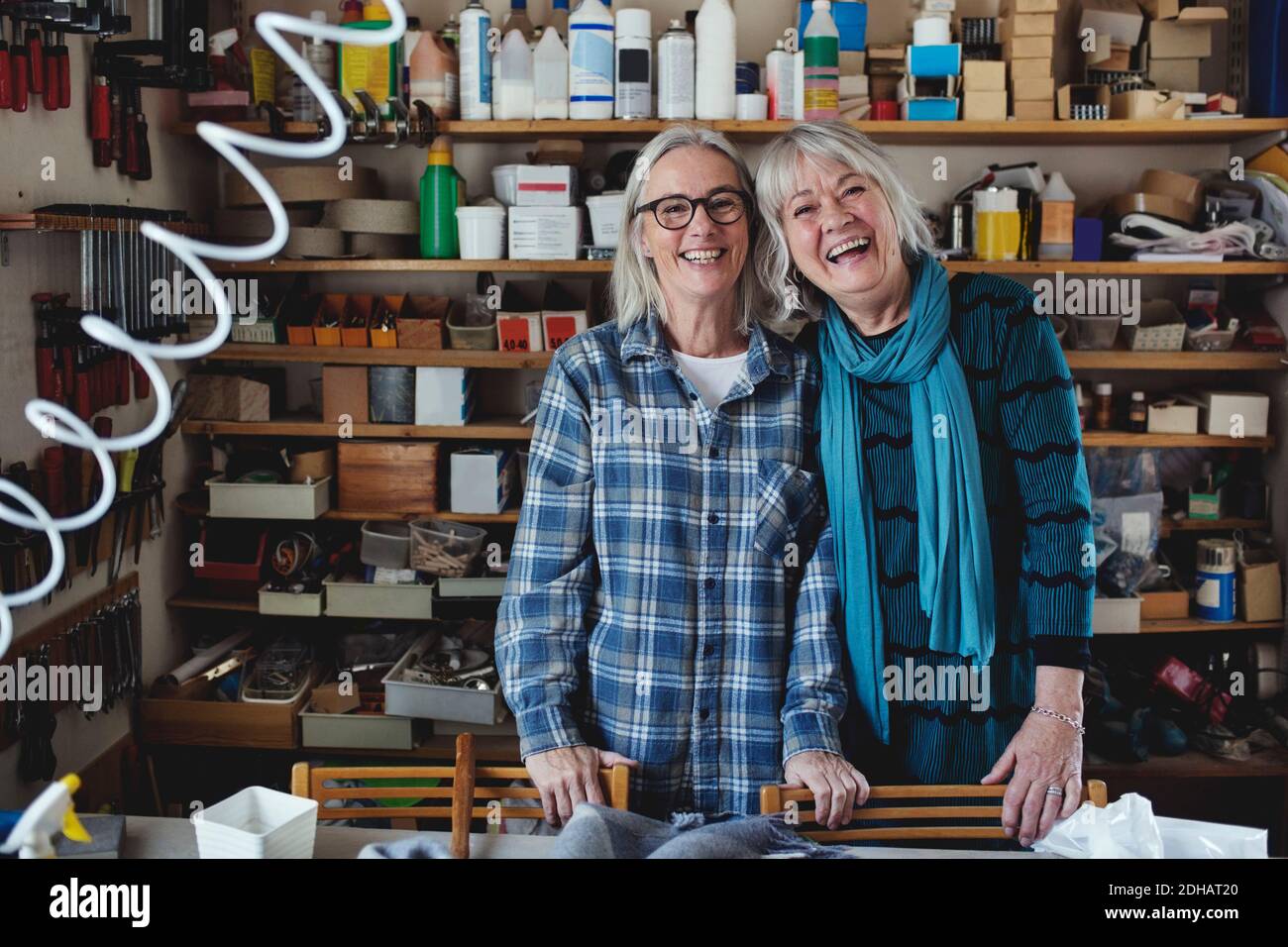 Portrait of cheerful colleagues standing against shelf at workshop ...