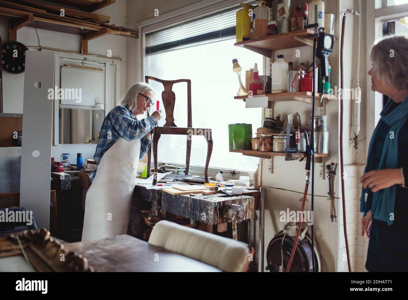 Female colleague looking at owner making chair in workshop Stock Photo ...