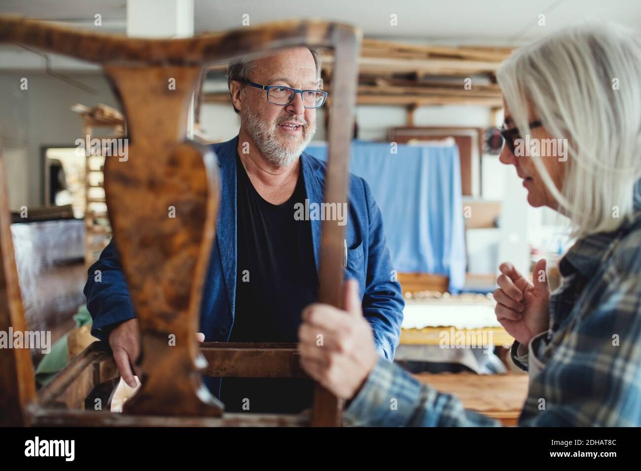 Senior owner showing wooden chair to male customer at workshop Stock ...