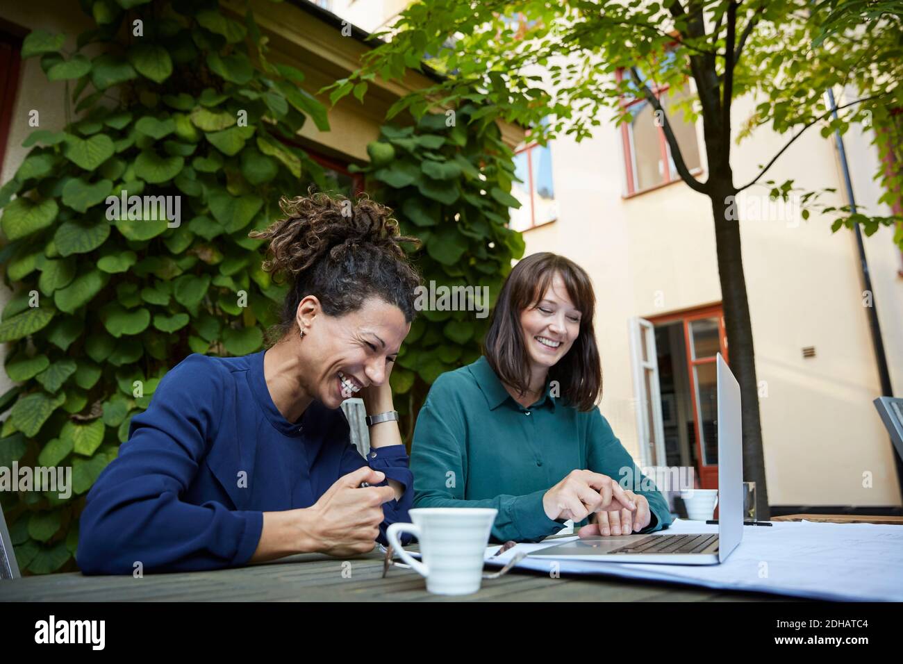 Female architects smiling while working at table in backyard Stock ...