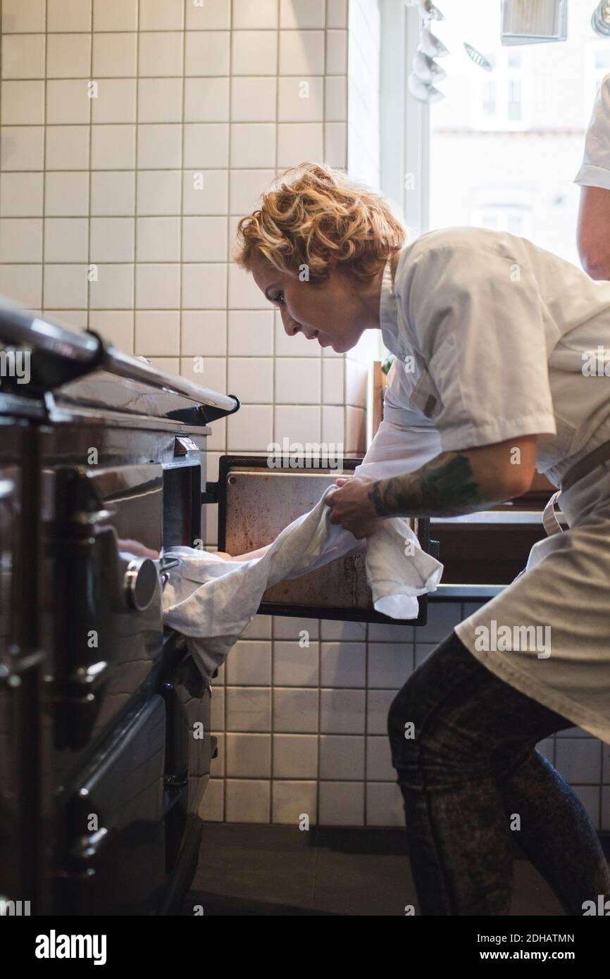 Side view of female chef using oven in restaurant kitchen Stock Photo ...