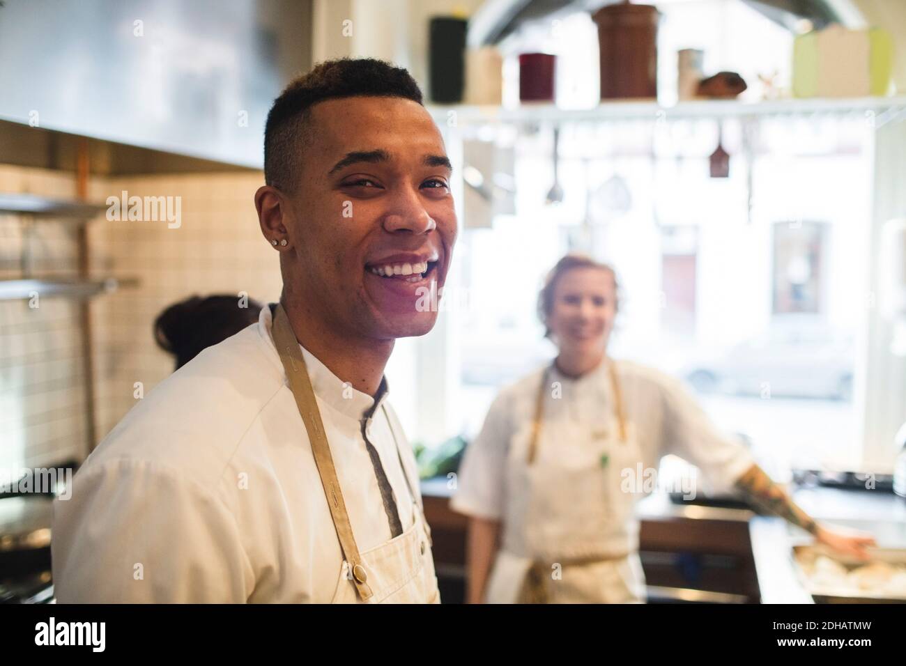 Portrait of smiling young chef standing in restaurant kitchen with ...
