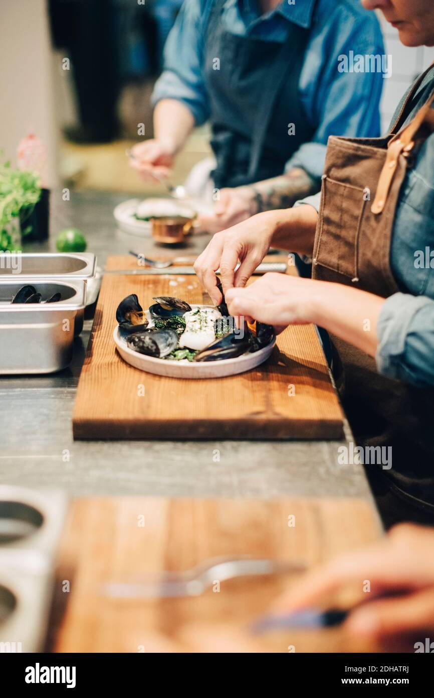 Midsection of chefs preparing food in plate on counter at restaurant ...