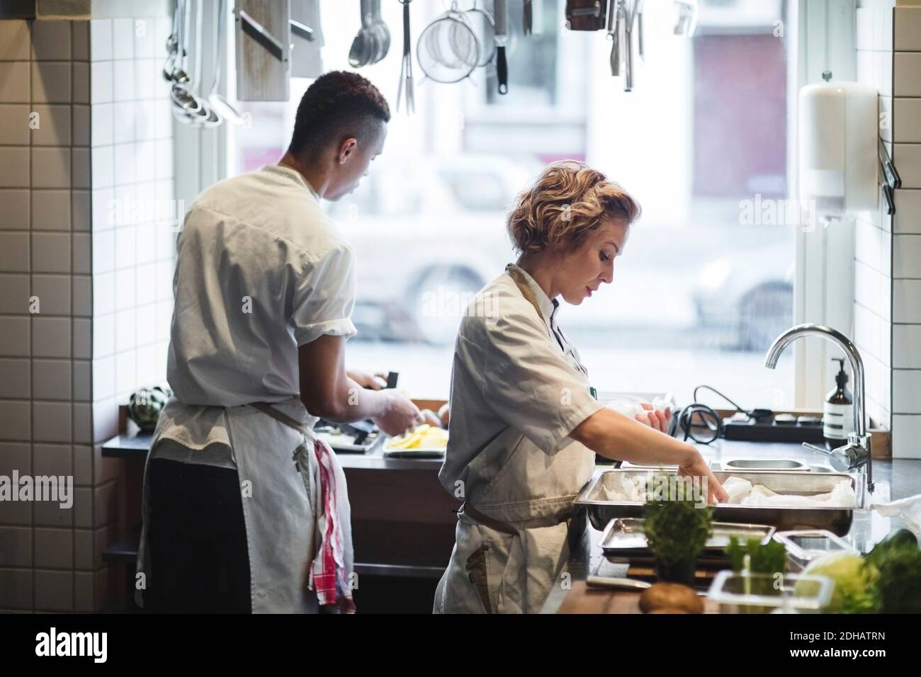 Side view of female chef preparing food on counter in kitchen with male ...
